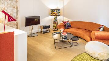 Uma sala de estar moderna com televisão de tela plana, luminária de chão vermelha, pintura abstrata colorida, sofá laranja e mesa de centro redonda.
