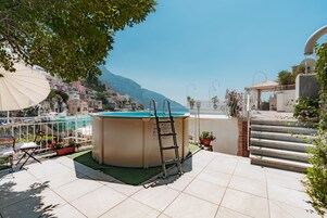 Uma área de piscina com escada, mobiliário de exterior e vista para uma vila na colina.