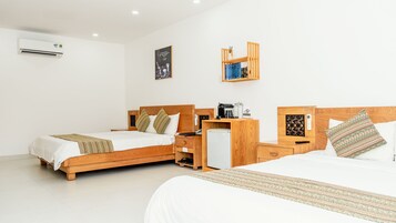 Quarto de hotel com duas camas de madeira, uma pequena mesa de trabalho com cafeteira, um frigorífico e uma estante com livros e um objeto decorativo.