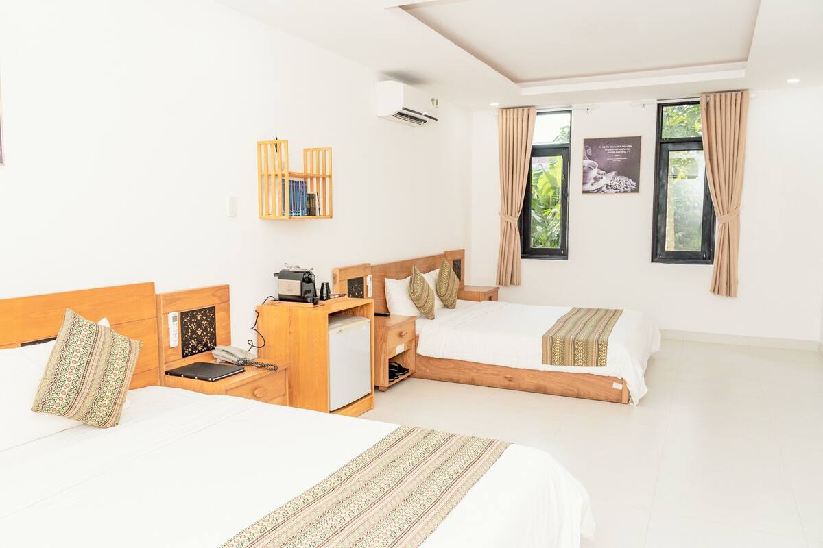 Quarto de hotel com duas camas, uma escrivaninha, mini-geladeira e estante de livros.