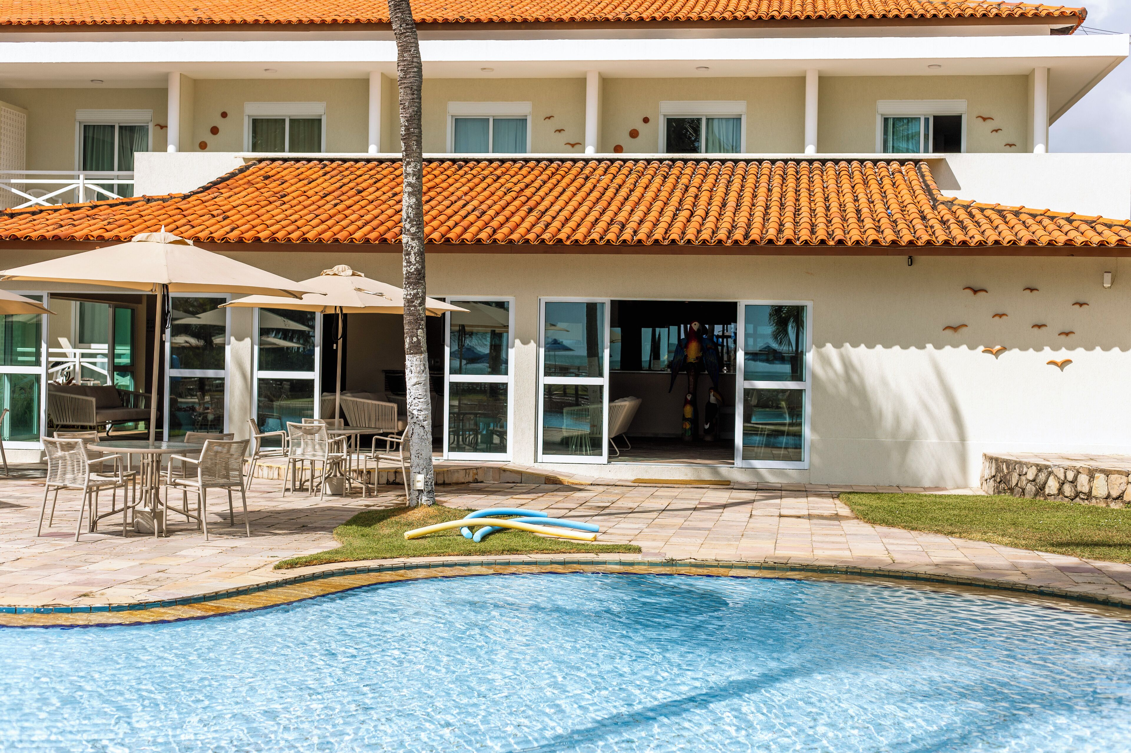 Um edifício de dois andares com piscina, área de estar ao ar livre e telhado em azulejo.