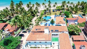 Vista aérea de um resort com piscina, acesso à praia e palmeiras.