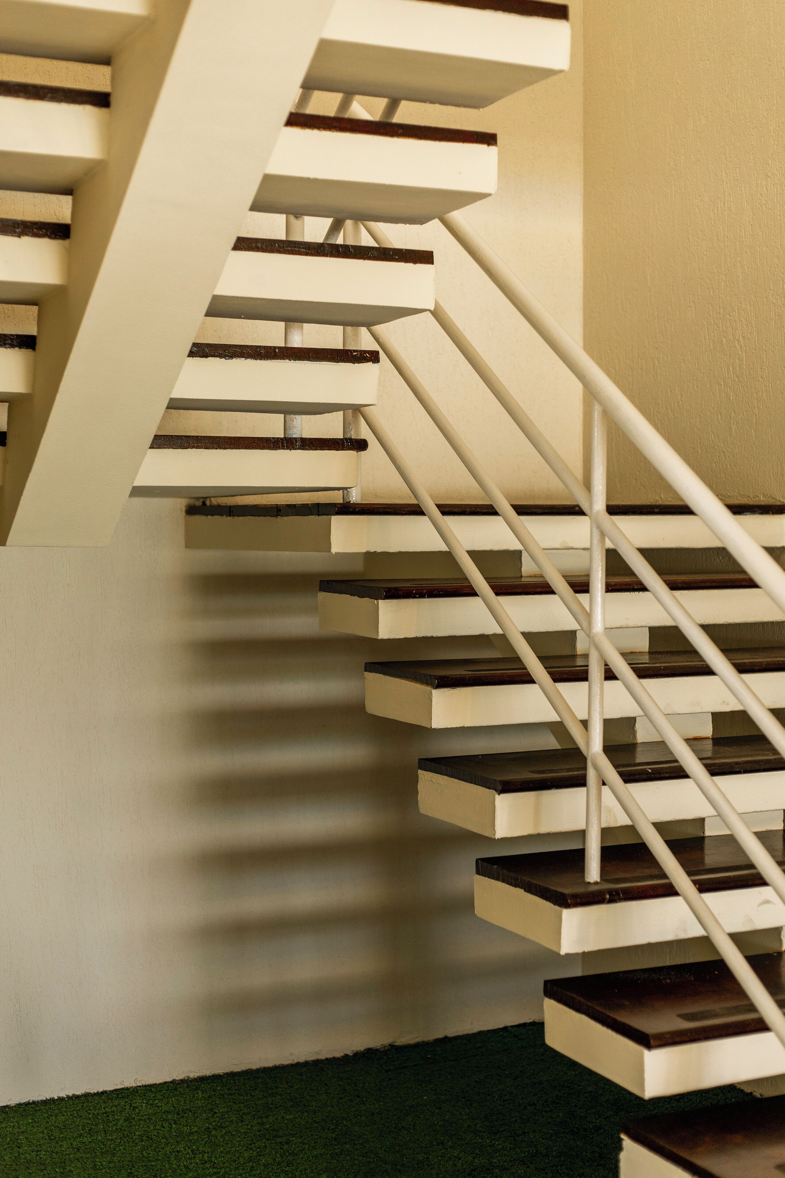 Uma escadaria em espiral com guarda-corrimãos brancos e degraus escuros, subindo em um ambiente interno moderno.