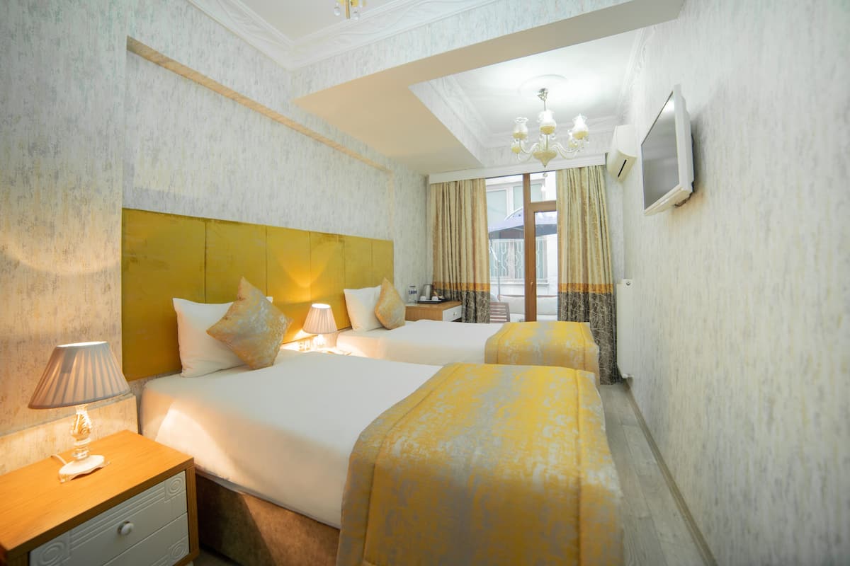 Quarto de hotel com duas camas, uma TV, uma luminária e uma janela com cortinas.