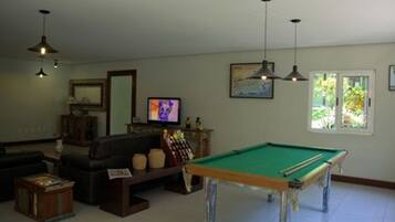Uma sala de estar com mesa de bilhar, televisão e sofá.