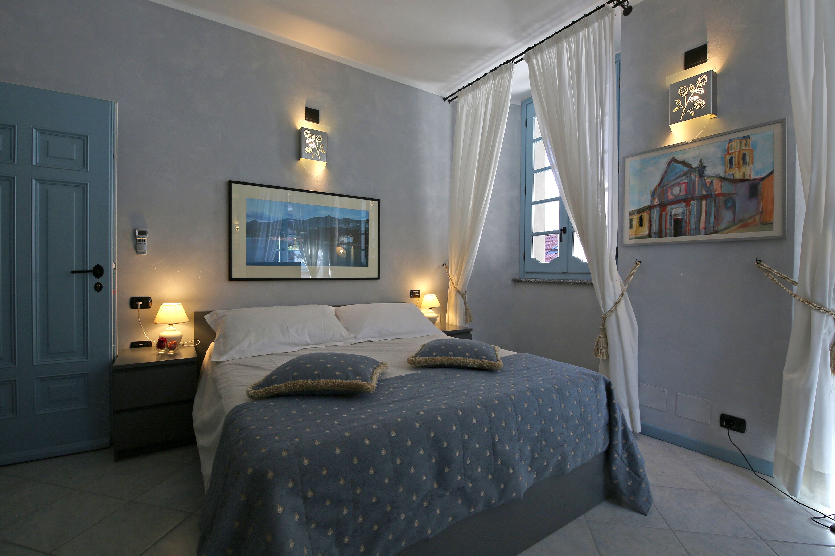 Um quarto com cama, luminárias de cabeceira, uma porta e um quadro na parede.