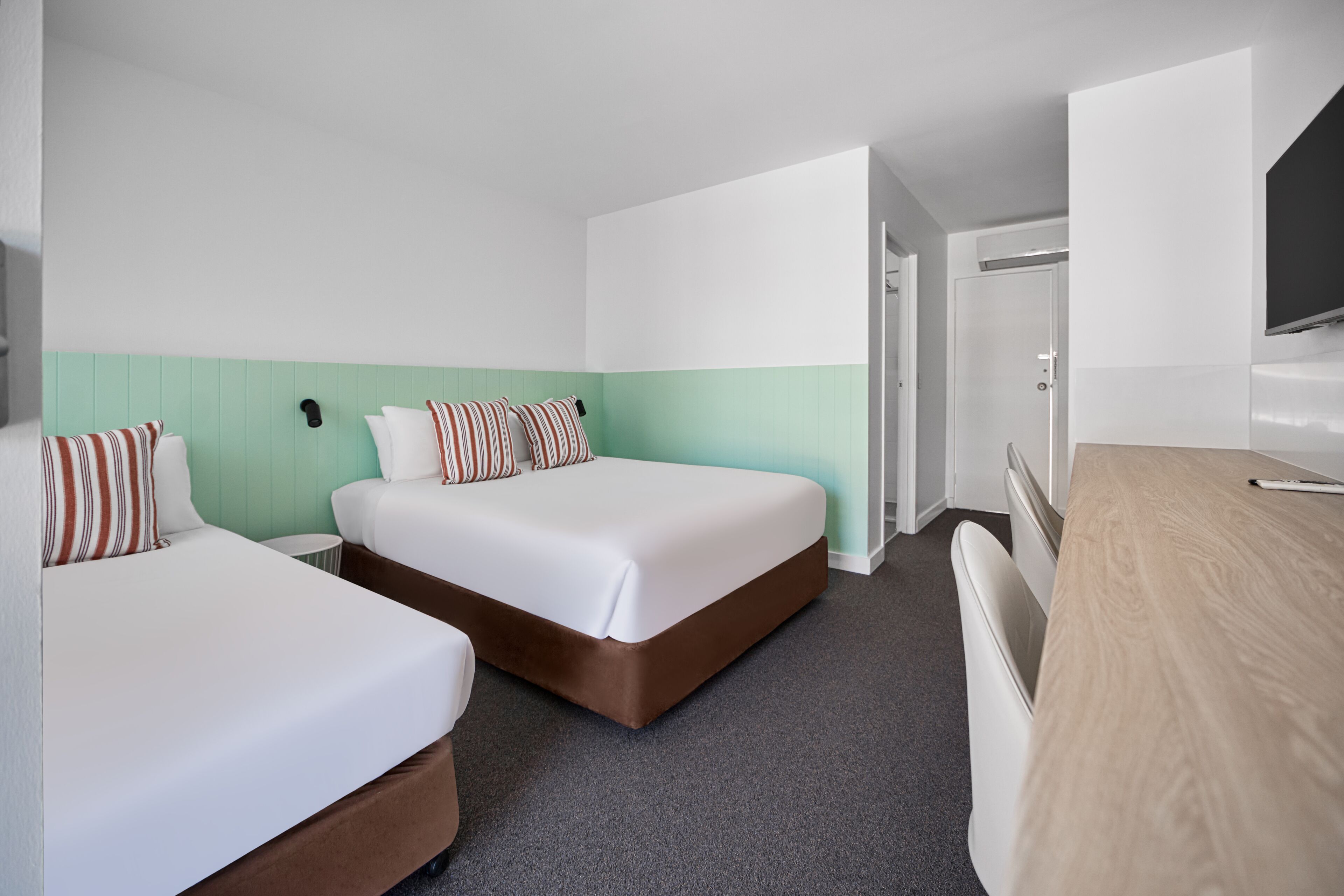 Quarto de hotel com duas camas, uma escrivaninha e uma televisão.