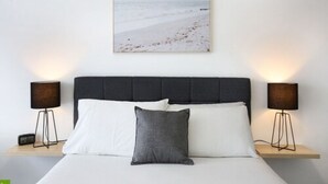 Quarto com uma cama, duas luminárias de cabeceira, um quadro emoldurado na parede e uma mesinha de cabeceira com uma luminária.