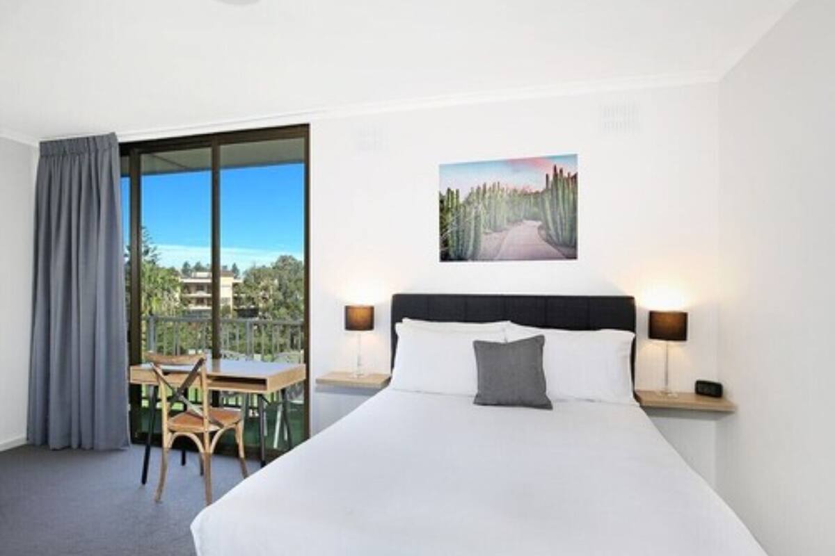 Quarto de hotel com uma cama grande, uma escrivaninha com cadeira, varanda com vista e um quadro na parede.