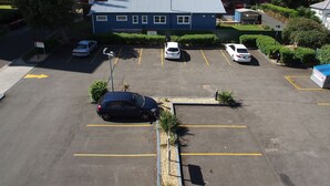 Um estacionamento com vários carros, um edifício azul com telhado vermelho e uma palmeira.