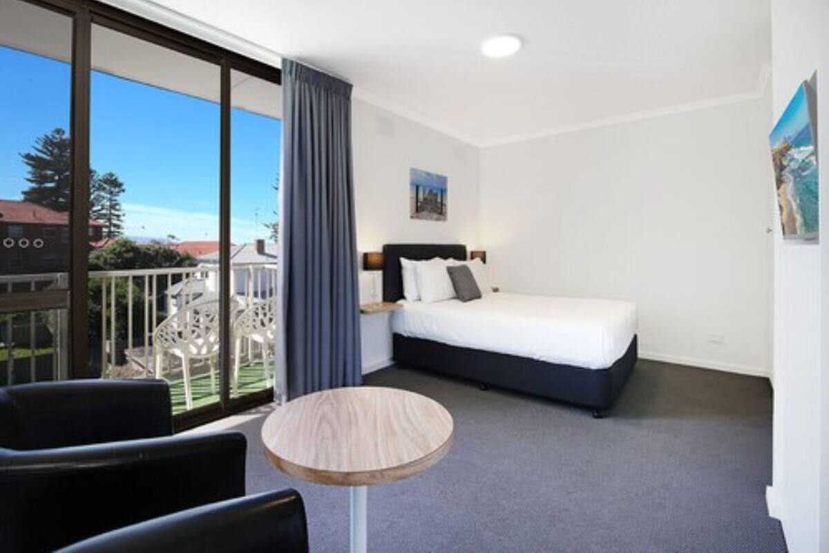 Quarto de hotel com uma cama, uma mesinha redonda e varanda com vista para edifícios.