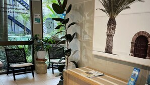 Uma área de recepção com balcão de madeira, plantas em vasos e vista para o exterior.