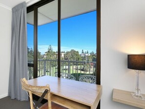 Varanda com mesa, cadeiras, luminária e vista para edifícios e árvores.