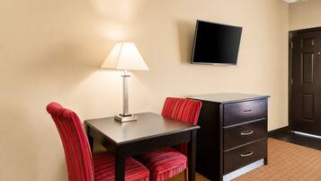 Quarto de hotel com escrivaninha, cadeira, luminária, televisão e guarda-roupa.