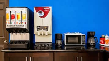 Uma bancada de cozinha com um dosador de suco Sunkist, uma máquina de café Nescafé, um micro-ondas e uma cafeteira.