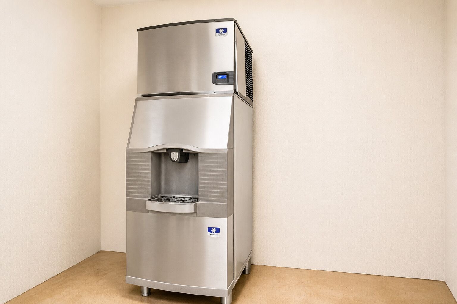 Máquina de café comercial de aço inoxidável num canto, com chão bege e paredes brancas.