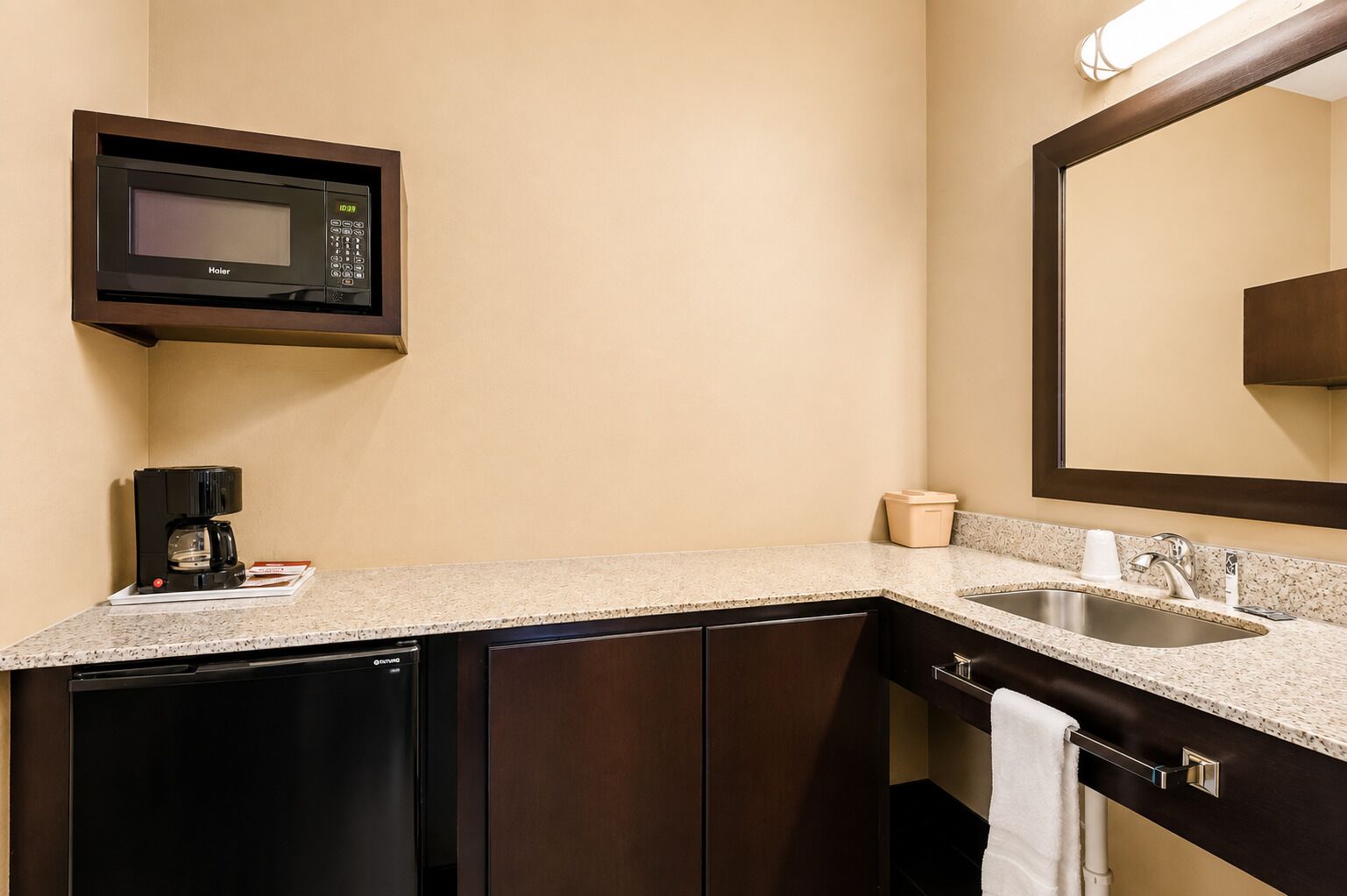Casa de banho de hotel compacta com micro-ondas embutido, máquina de café, pia e um espelho grande.