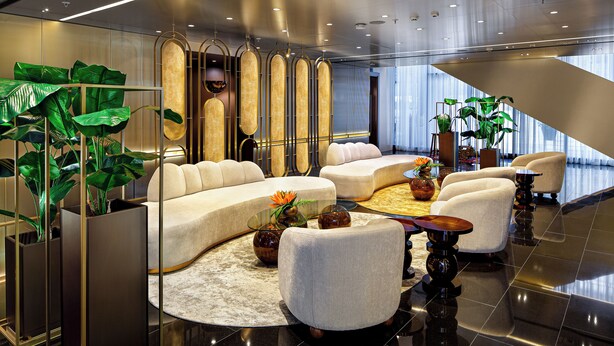 Um interior moderno com um sofá curvo, poltronas, uma mesa de centro e grandes vasos de plantas.