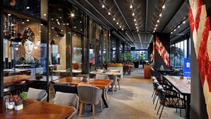 Um restaurante moderno com tetos altos, luminárias pendentes e amplas janelas com vista para a cidade.