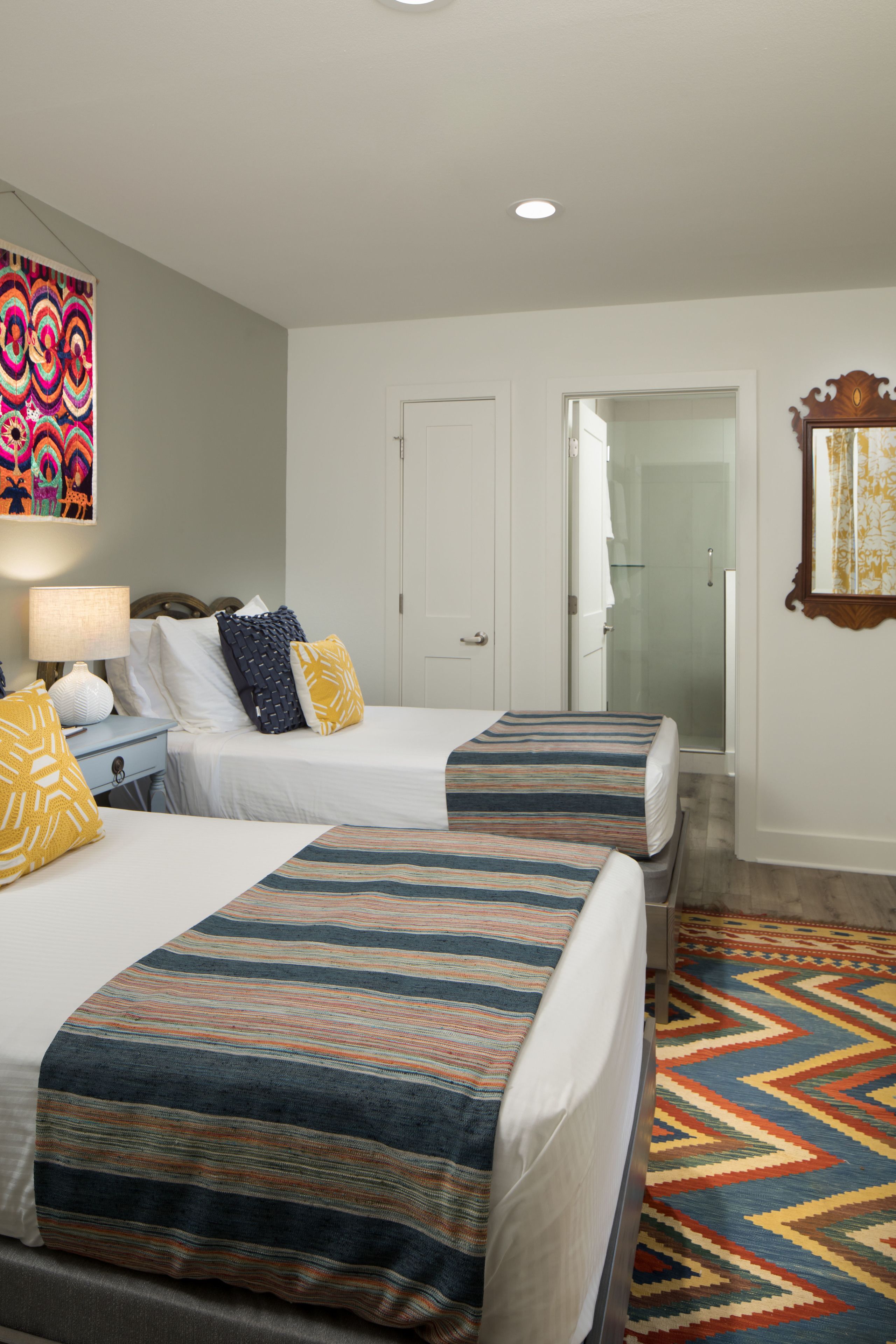 Quarto de hotel com duas camas, um tapete estampado, um quadro na parede e uma porta para o banheiro.