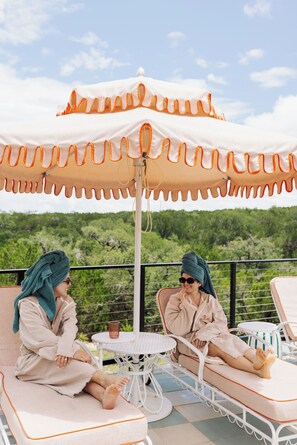 Duas cadeiras de descanso com um guarda-sol branco e laranja, uma mesinha e vista para o verde.