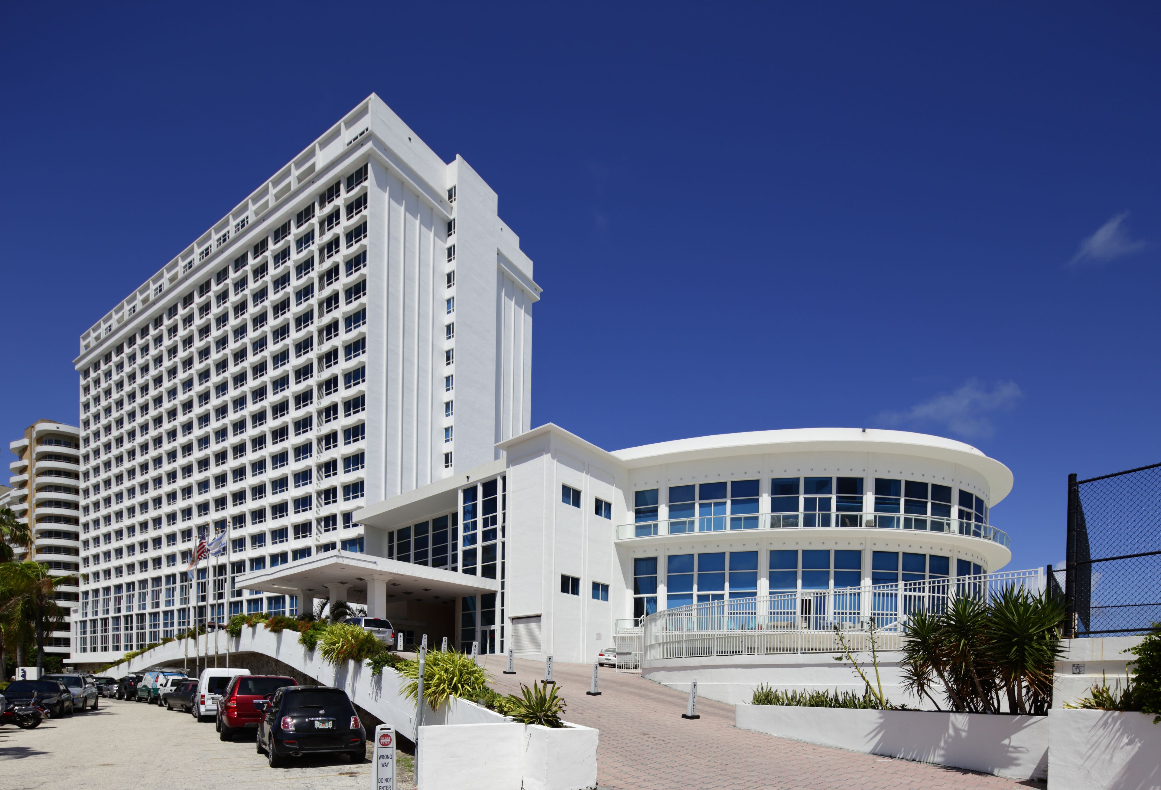 Um hotel grande com vários andares, um edifício curvo e um estacionamento cheio de carros.