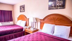 Quarto de hotel com duas camas, cada uma com cabeceira de madeira, uma mesinha de cabeceira com luminária e ar-condicionado fixado na parede.