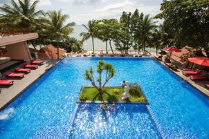 Piscina com ilha central, cadeiras de descanso vermelhas e palmeiras.