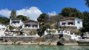 Uma propriedade costeira com edifícios brancos, águas azul-turquesa cristalinas e terreno rochoso.