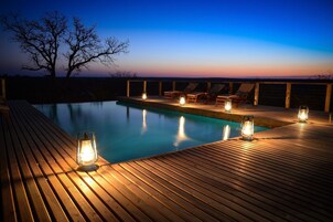 Um deck de madeira com piscina, espreguiçadeiras e lanternas.