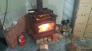 Uma lareira a lenha com fogo aceso, rodeada por uma estrutura de tijolos e toras de madeira.