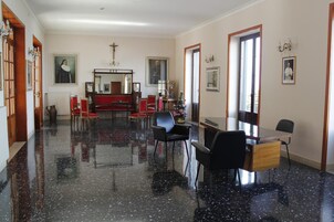 Um quarto amplo com piso preto polido, uma escrivaninha de madeira com cadeiras, um sofá vermelho e um espelho grande.
