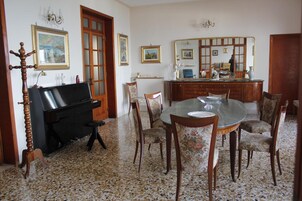 Uma sala de jantar com piano, mesa de vidro redonda e cadeiras florais.