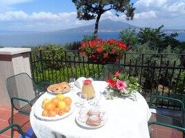 Mesa de varanda posta com itens de café da manhã, vista para uma montanha e um corpo d'água.