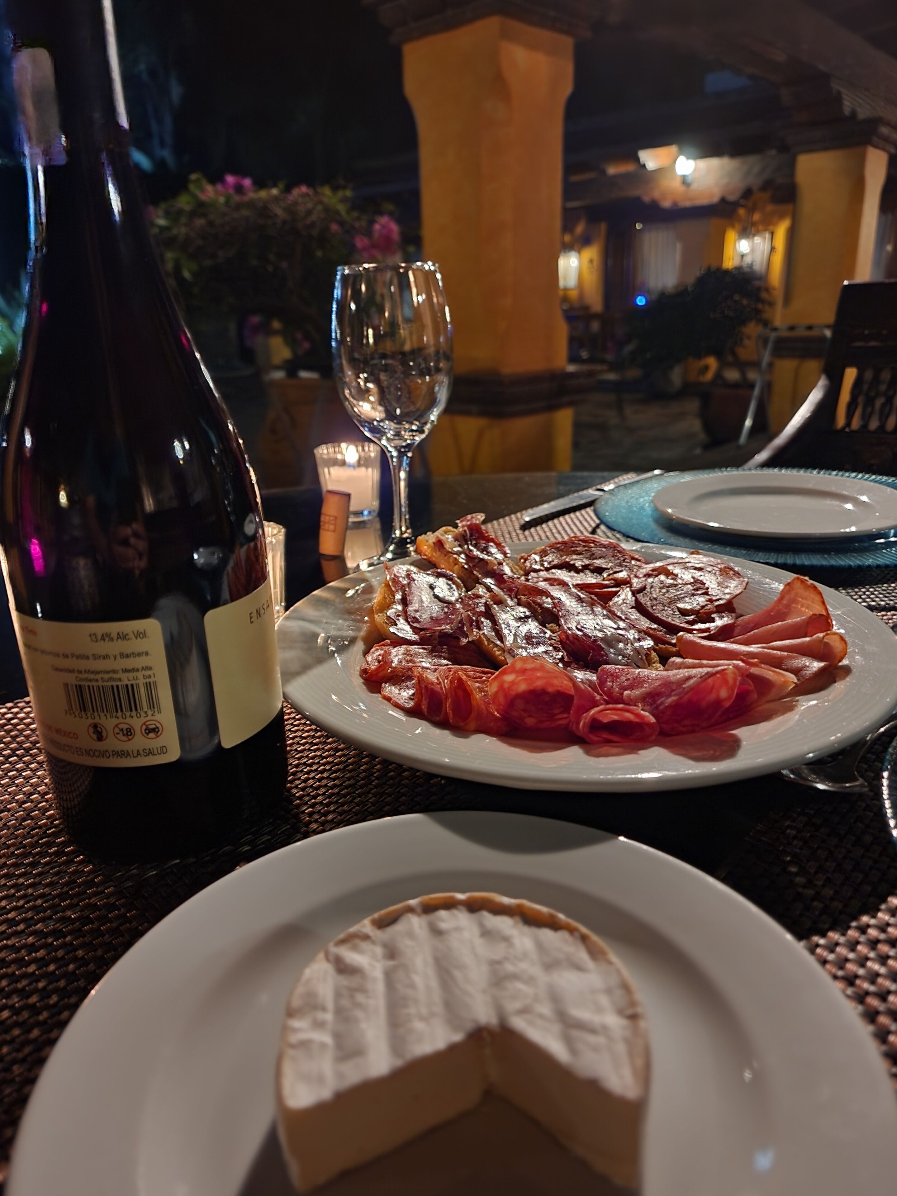 Uma mesa posta com uma garrafa de vinho, um copo e pratos de comida, incluindo charcutaria e queijo.