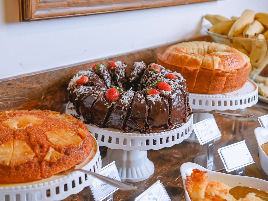 Diversos doces à mostra, incluindo um bolo de chocolate com morangos e um bolo de abacaxi invertido.
