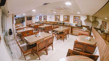 Um restaurante com várias mesas e cadeiras de madeira, um balcão de buffet e obras de arte nas paredes.