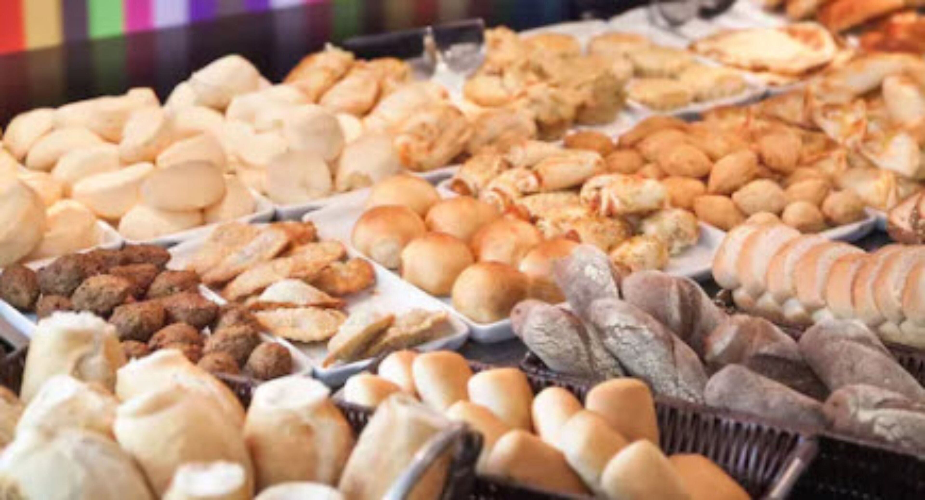 Diversos produtos de panificação, como pão, bolos e biscoitos, expostos em bandejas.