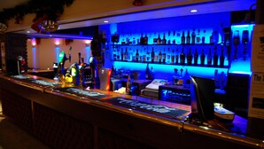 Uma área de bar com balcão, prateleiras cheias de garrafas e um letreiro de neon.