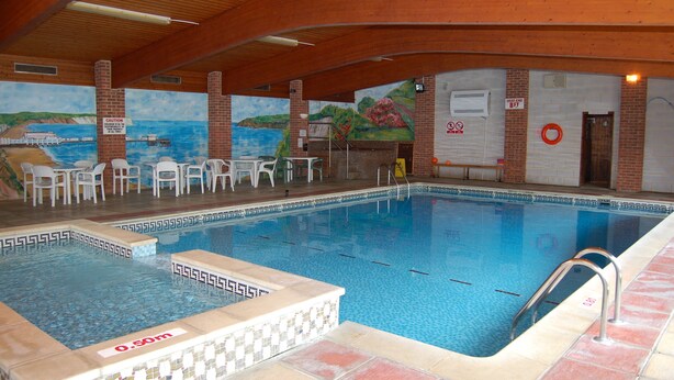 Piscina interior com placa de segurança, boia salva-vidas e um mural de paisagem costeira.