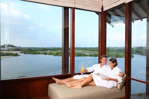 Um casal relaxando em um banco acolchoado perto de uma janela grande com vista para um rio.