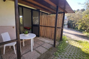 Um alpendre coberto com mesa e cadeiras, cerca de bambu e um caminho pavimentado.