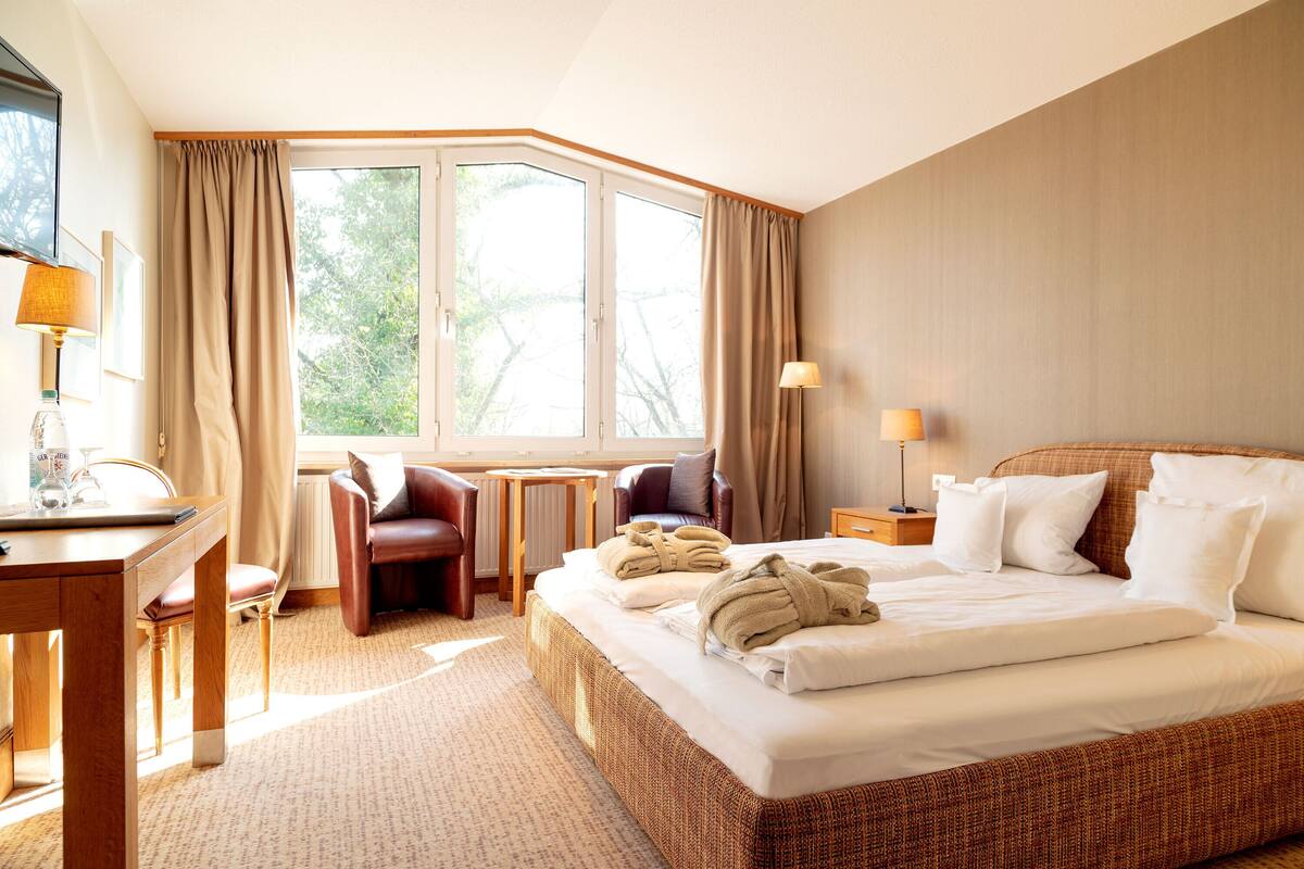 Quarto de hotel com uma cama grande, uma escrivaninha, uma cadeira e uma janela com cortinas.