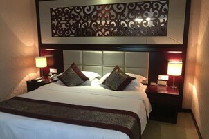 Quarto de hotel com uma cama grande, duas mesas de cabeceira e painéis decorativos na parede.
