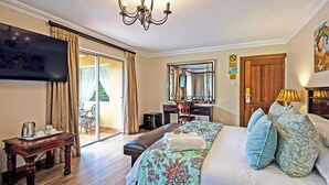 Quarto de hotel com cama, escrivaninha, cadeira, televisão e porta de vidro corrediça para a varanda.