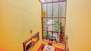 Um quarto com uma janela grande, uma mesa de jantar, cadeiras e um espelho.