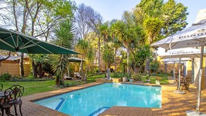 Piscina com deck revestido, rodeada por vegetação e mobiliário de exterior.