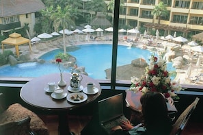 Vista de uma área de piscina com espreguiçadeiras e guarda-sóis, uma mesa de jantar com um vaso de flores e um laptop sobre a mesa.
