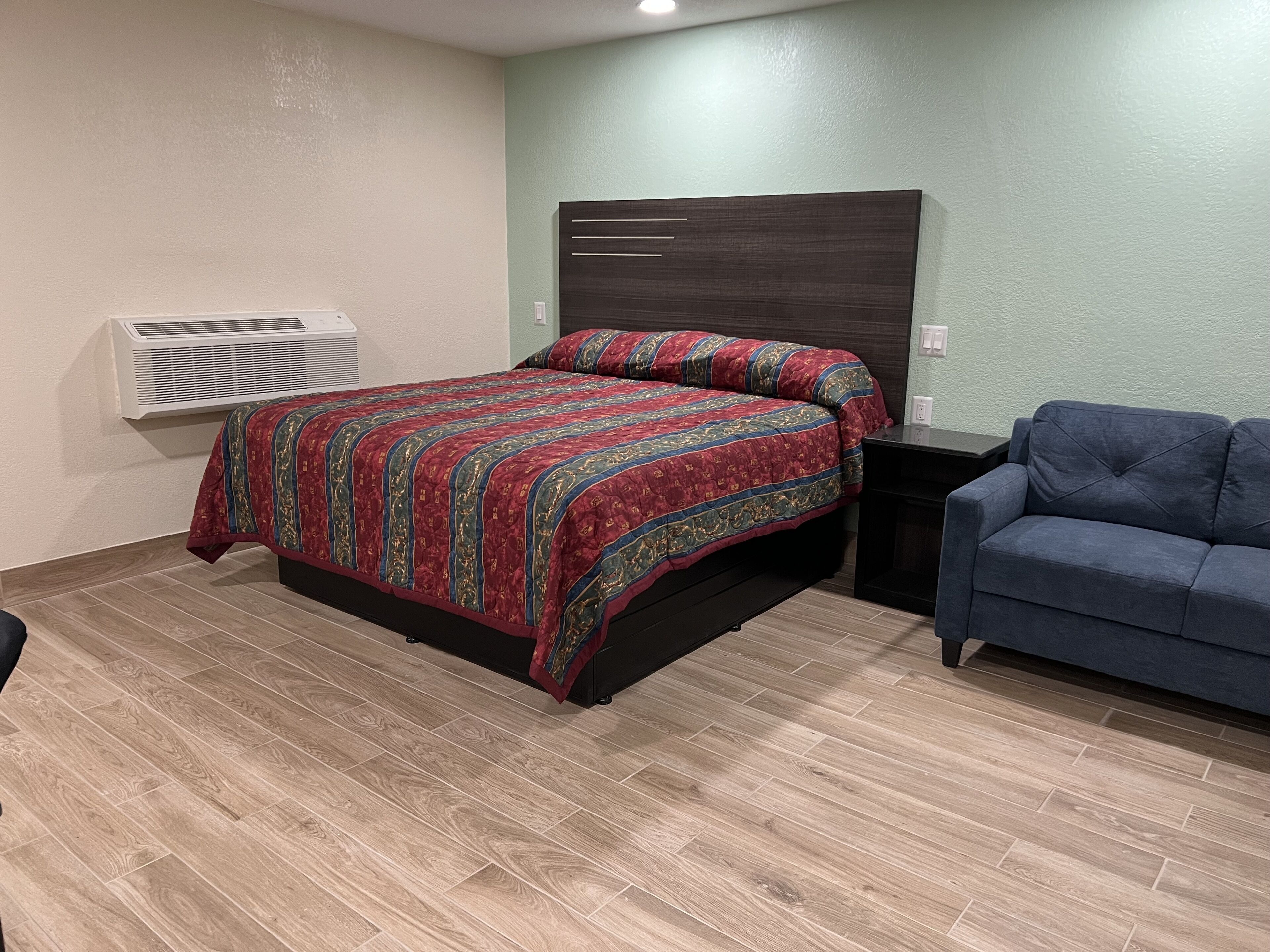 Quarto com cama, sofá azul e ar-condicionado fixado na parede.