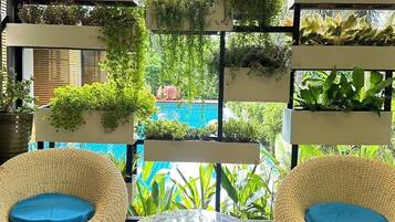 Uma área de estar moderna ao ar livre, com cadeiras de vime e uma mesa de vidro, rodeada por estantes de jardim vertical e vista para uma piscina.